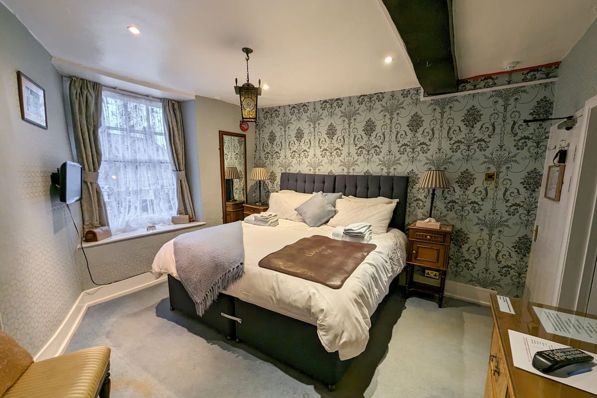 Quarto bem arrumado com uma cama grande, abajures, uma janela com cortinas e um relógio fixado na parede.