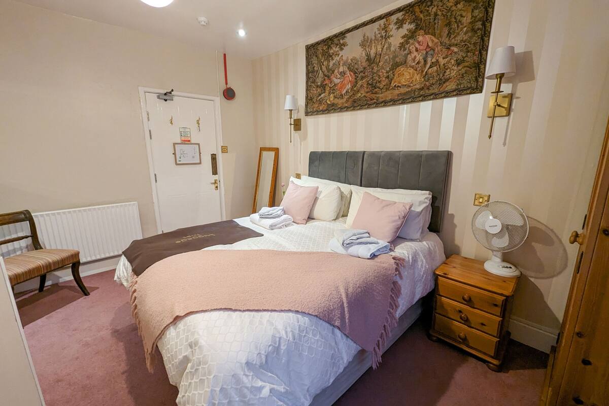 Quarto com cama, mesa de cabeceira, abajur e um quadro na parede.