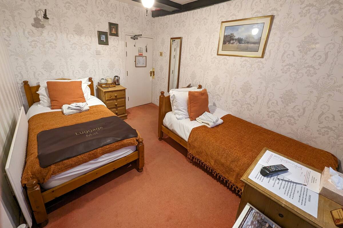 Quarto de hotel com duas camas, uma cômoda de madeira, um espelho e um quadro pendurado na parede.