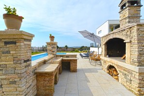 Um pátio externo com construção em pedra, piscina, área de churrasco e espaço para sentar.