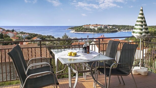 Varanda com mesa posta para dois, vista para a costa com um edifício e barcos.