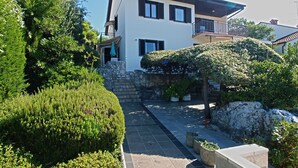 Uma casa moderna de dois andares, com uma escadaria de pedra que leva a uma varanda.