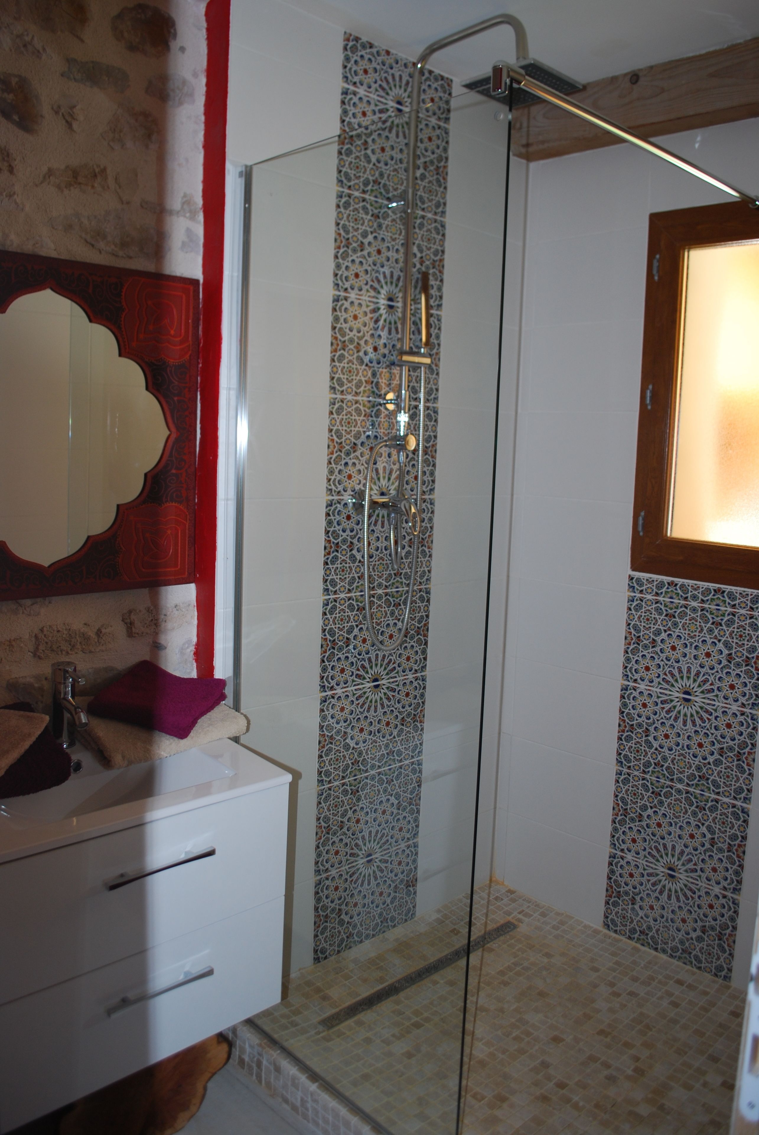 Uma casa de banho com cabine de duche em vidro, uma sanita branca e azulejos estampados.