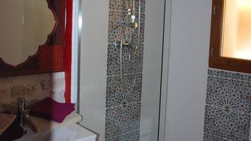 Uma casa de banho com cabine de duche em vidro, uma sanita branca e azulejos estampados.