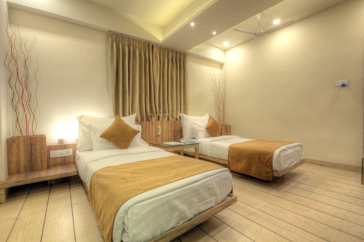 Quarto de hotel com duas camas, uma mesa de cabeceira, uma pequena mesa e um ventilador de teto.
