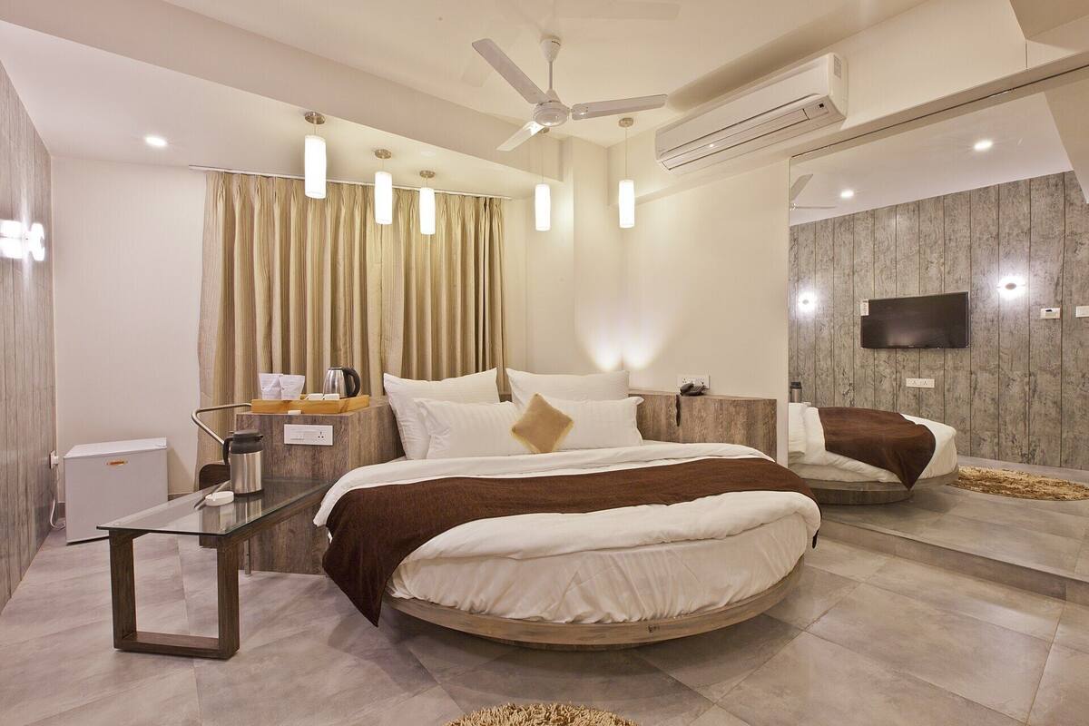 Quarto moderno com uma cama grande, uma mesa de vidro, um ventilador de teto e uma TV na parede.