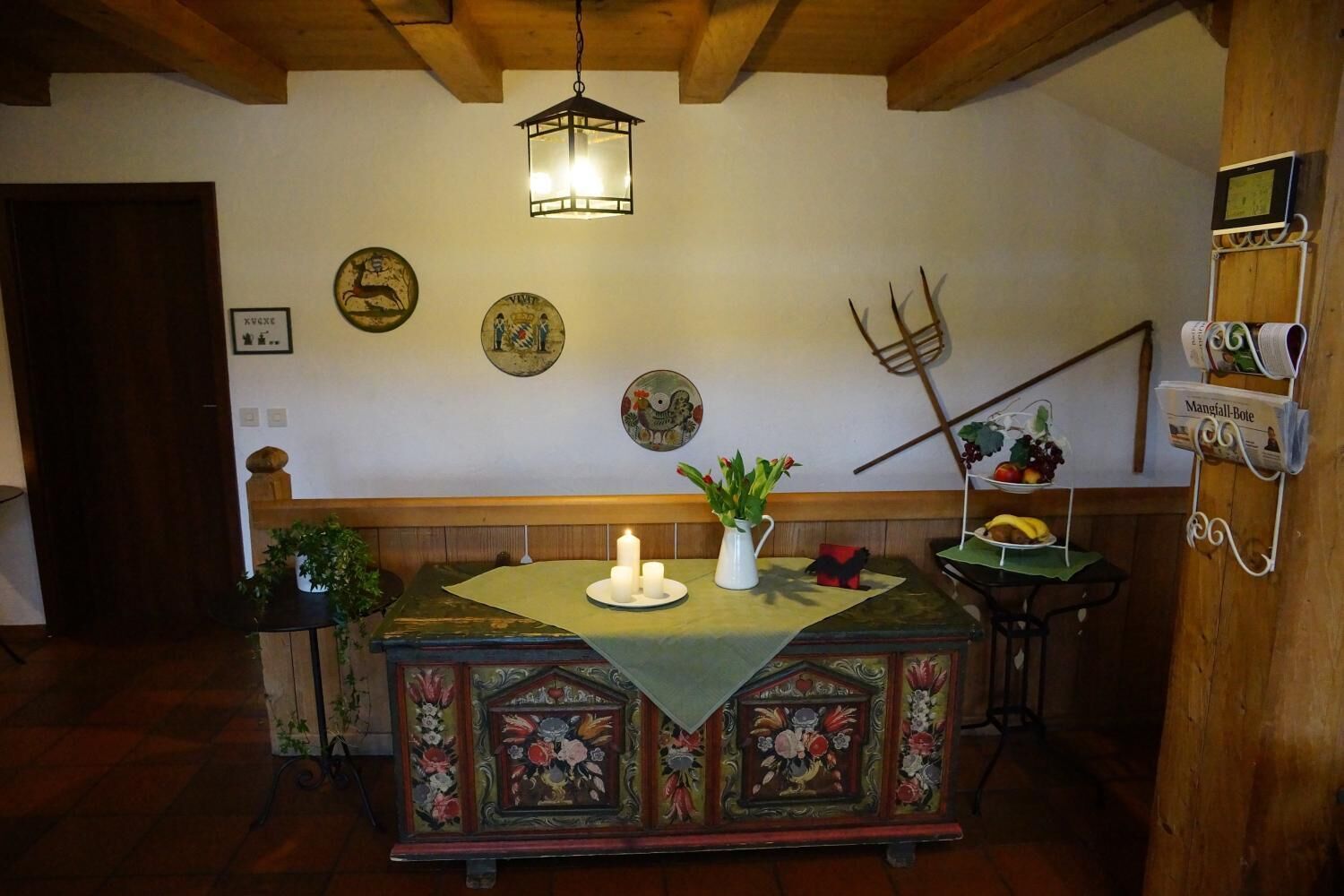 Uma área de jantar rústica com uma mesa de madeira posta para dois, um arranjo de velas e um aparador decorativo com motivos florais.