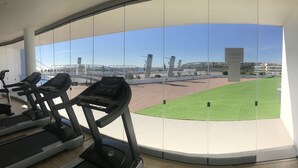 Uma academia com esteiras e vista para um campo esportivo.