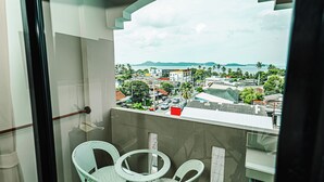 Varanda com duas cadeiras de vime branco e uma mesa pequena, com vista para um horizonte urbano com edifícios, palmeiras e um corpo de água.