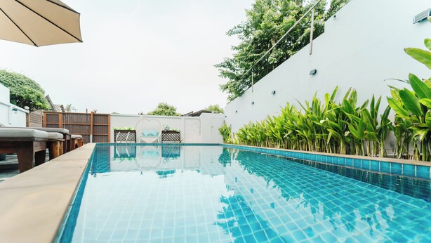 Piscina retangular com água azul cristalina, rodeada por um muro branco e vegetação verde exuberante.