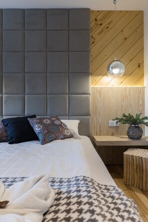 Um quarto moderno com cabeceira estofada, parede de destaque em madeira, mesa de cabeceira com planta e colcha estampada.