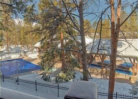 Área externa nevada com piscina, cercada por árvores e estruturas cobertas.
