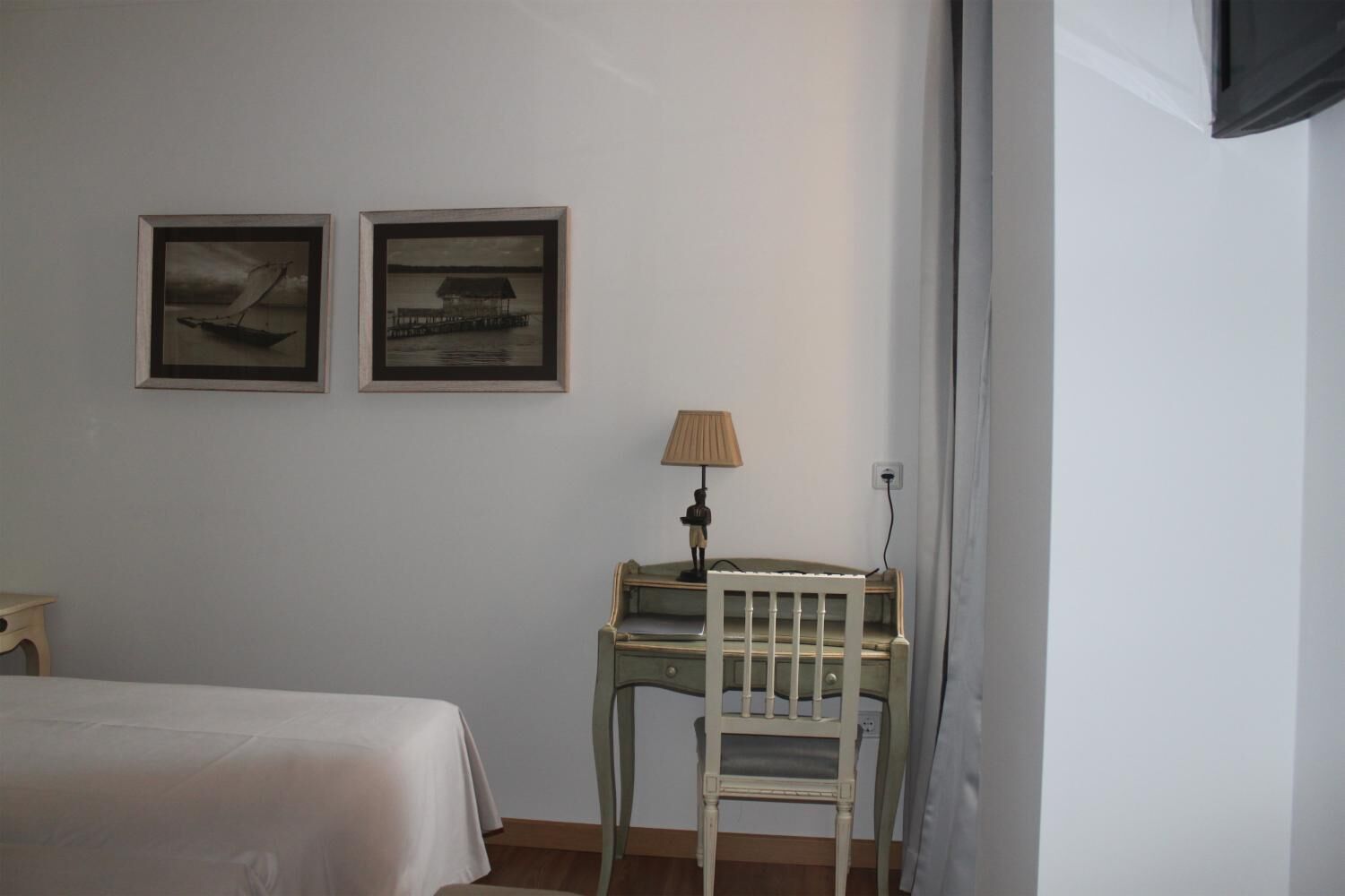 Um quarto com uma cama, uma escrivaninha com luminária e duas imagens emolduradas na parede.
