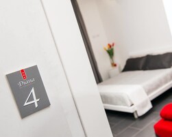 Quarto de hotel com uma cama, uma pequena mesa e um letreiro fixado na parede indicando o número 4.