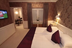 Quarto de hotel com uma cama grande, uma escrivaninha e uma televisão na parede.