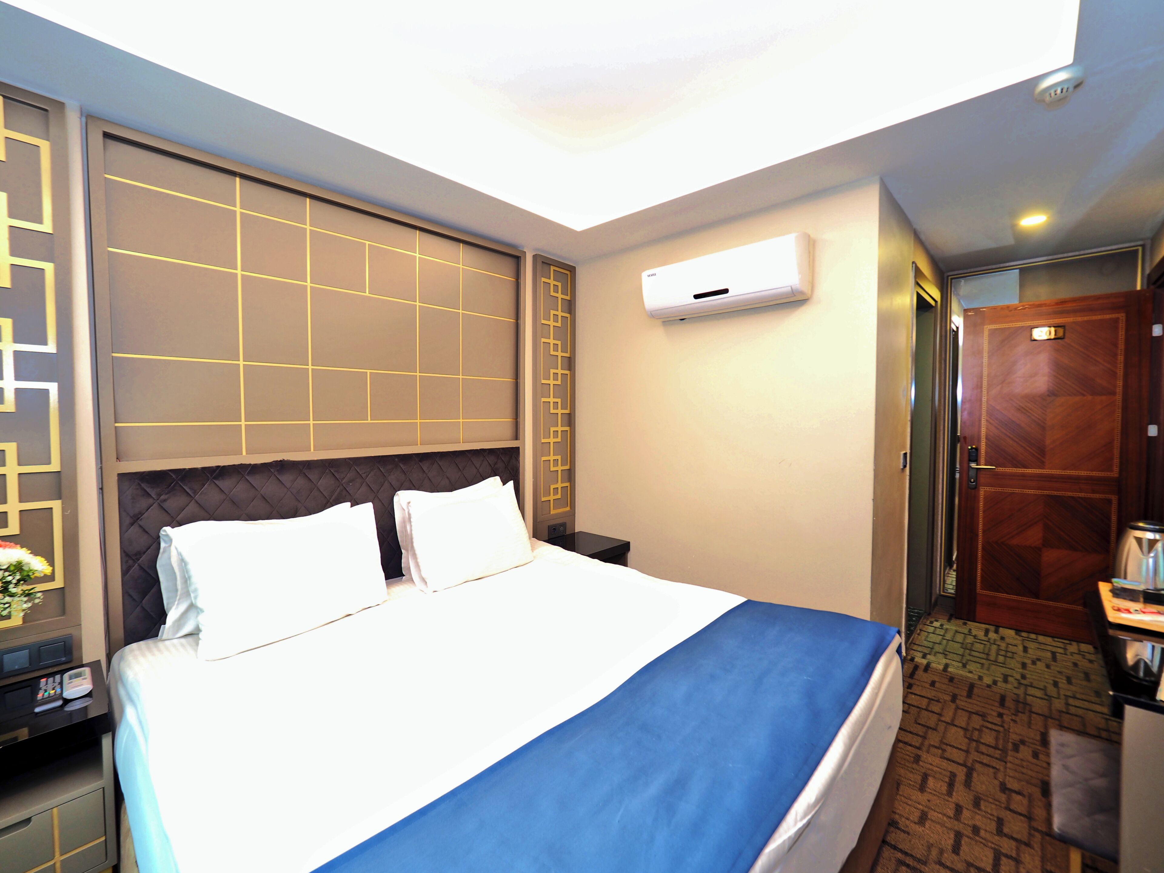 Quarto de hotel com cama, mesa de cabeceira, aparelho de ar condicionado e uma porta.