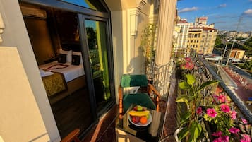 Uma varanda com uma cama, uma mesa de jantar com frutas e vista para a cidade.