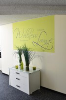 Uma mesa de recepção com uma placa indicando "Wellness Lounge" e um arranjo decorativo de plantas.