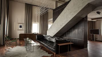 Uma sala de estar moderna com um sofá de couro preto, uma mesa de centro de vidro e uma escada com parede de concreto.