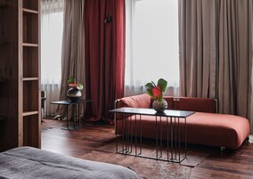 Uma sala de estar moderna com um sofá vermelho, duas mesinhas de centro com vasos, uma estante de madeira e uma grande janela com cortinas.