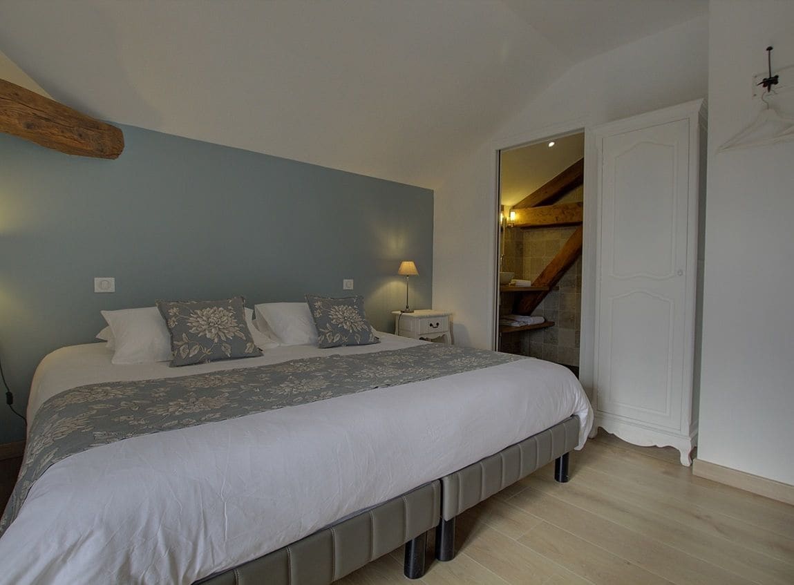 Quarto com uma cama grande, uma mesa de cabeceira, um abajur e um vigamento de madeira no teto.