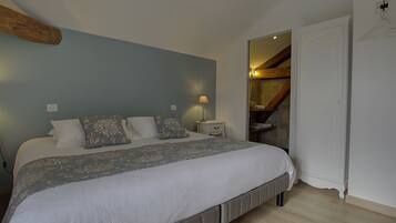 Quarto com uma cama grande, uma mesa de cabeceira, um abajur e um vigamento de madeira no teto.