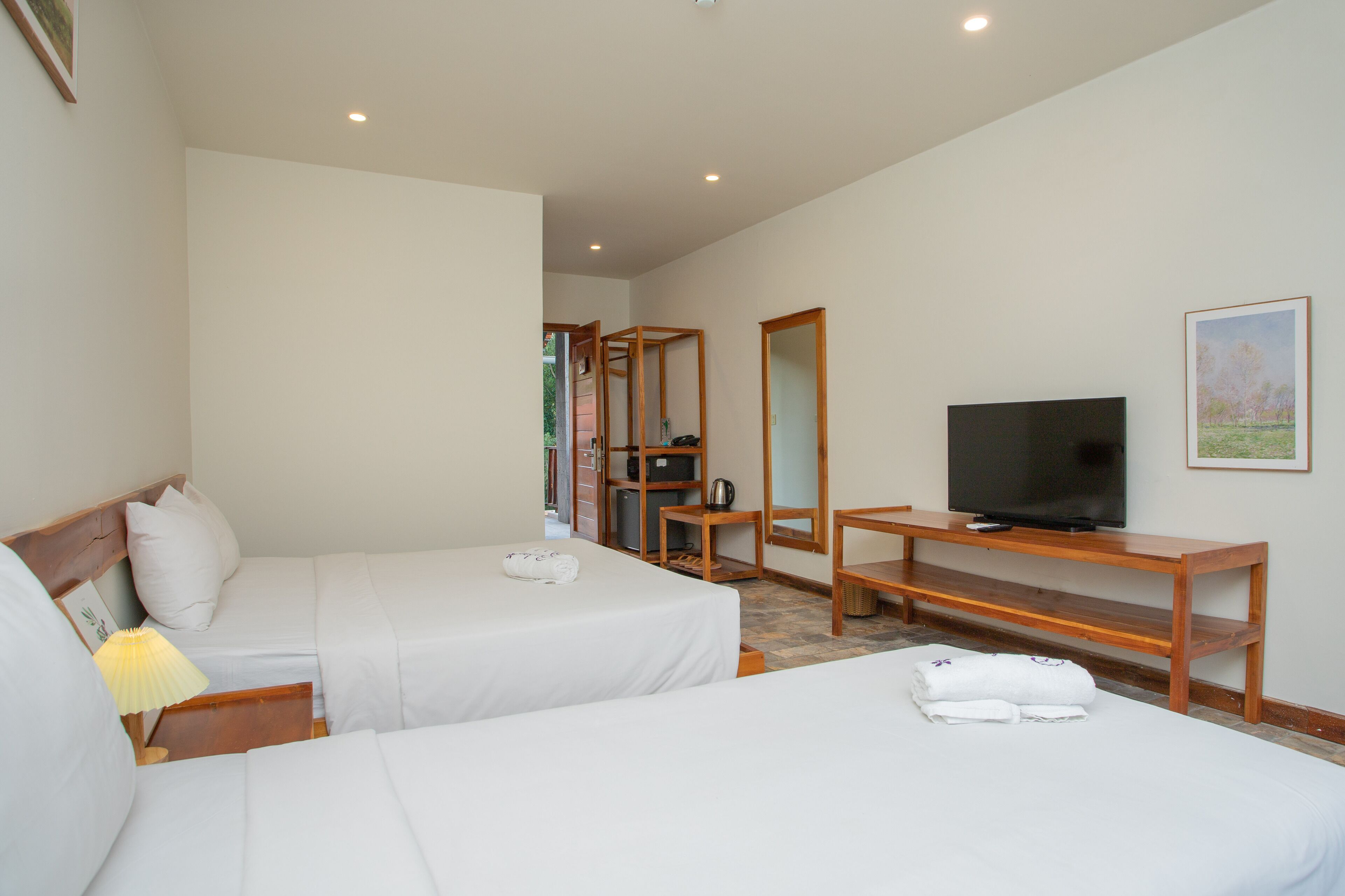 Quarto de hotel com duas camas de solteiro, televisão, um banco de madeira e um espelho.