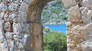 Um antigo arco de pedra com vista para um corpo de água azul e vegetação ao fundo.