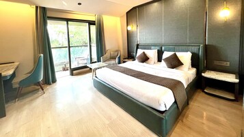 Quarto de hotel moderno com uma cama grande, área de estar com uma cadeira, uma pequena mesa e vista pela janela.