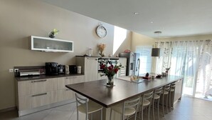 Cozinha moderna com ilha central, área de jantar com cadeiras e uma grande janela com cortinas.