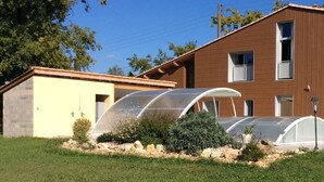 Uma casa de dois andares com fachada marrom, uma pequena garagem anexa e um jardim com estufa.