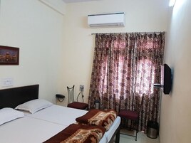 Quarto de hotel com cama, poltrona, ar condicionado, cortina, telefone fixado na parede e porta-retrato.