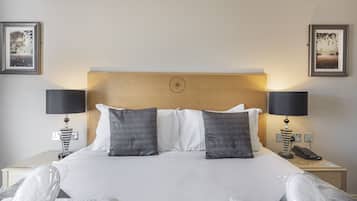 Cama bem arrumada com roupa de cama branca e cinza, duas luminárias de cabeceira e cabeceira de madeira com desenho de bússola.