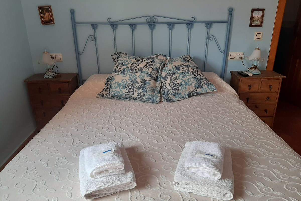 Cama bem arrumada com almofadas estampadas e duas toalhas dobradas.
