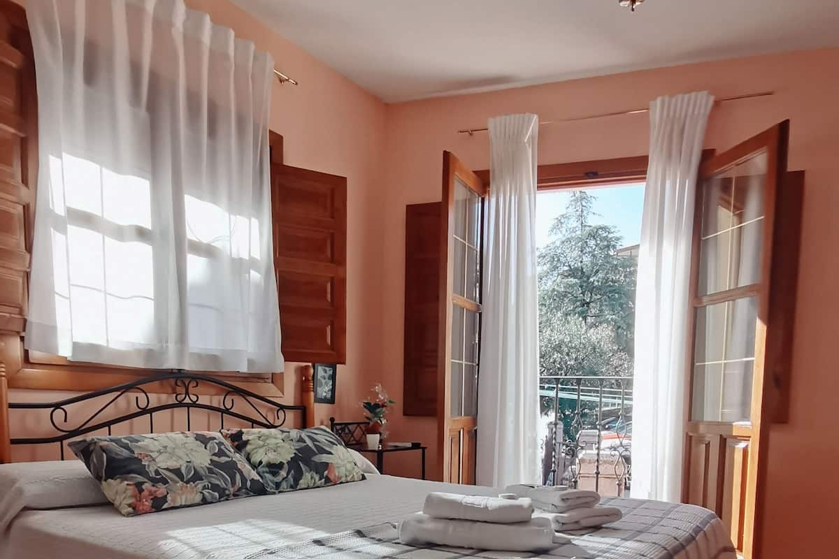 Quarto com cama, cortinas, um lustre e vista para o exterior.