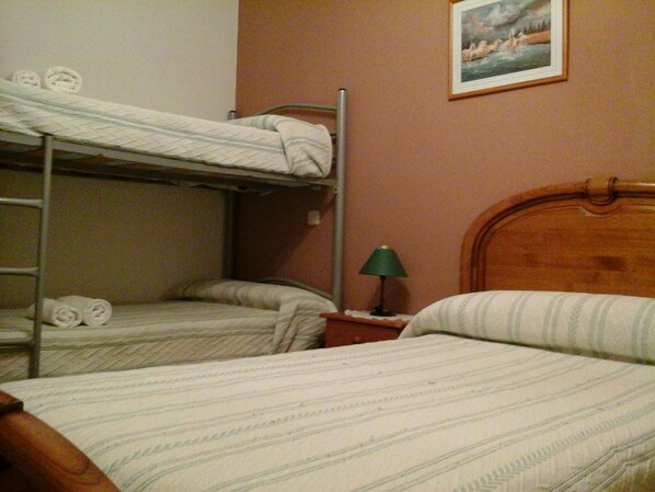 Um quarto com duas camas beliches, uma cabeceira de madeira, um abajur verde e um quadro na parede.