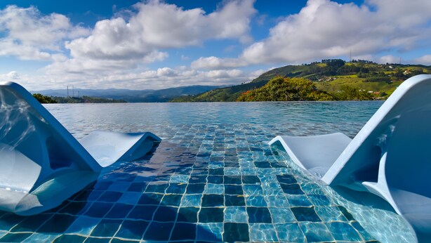 Uma piscina com água azul cristalina e vista para uma paisagem montanhosa ao fundo.