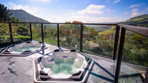 Duas banheiras de hidromassagem numa varanda com uma vista panorâmica de uma paisagem montanhosa.