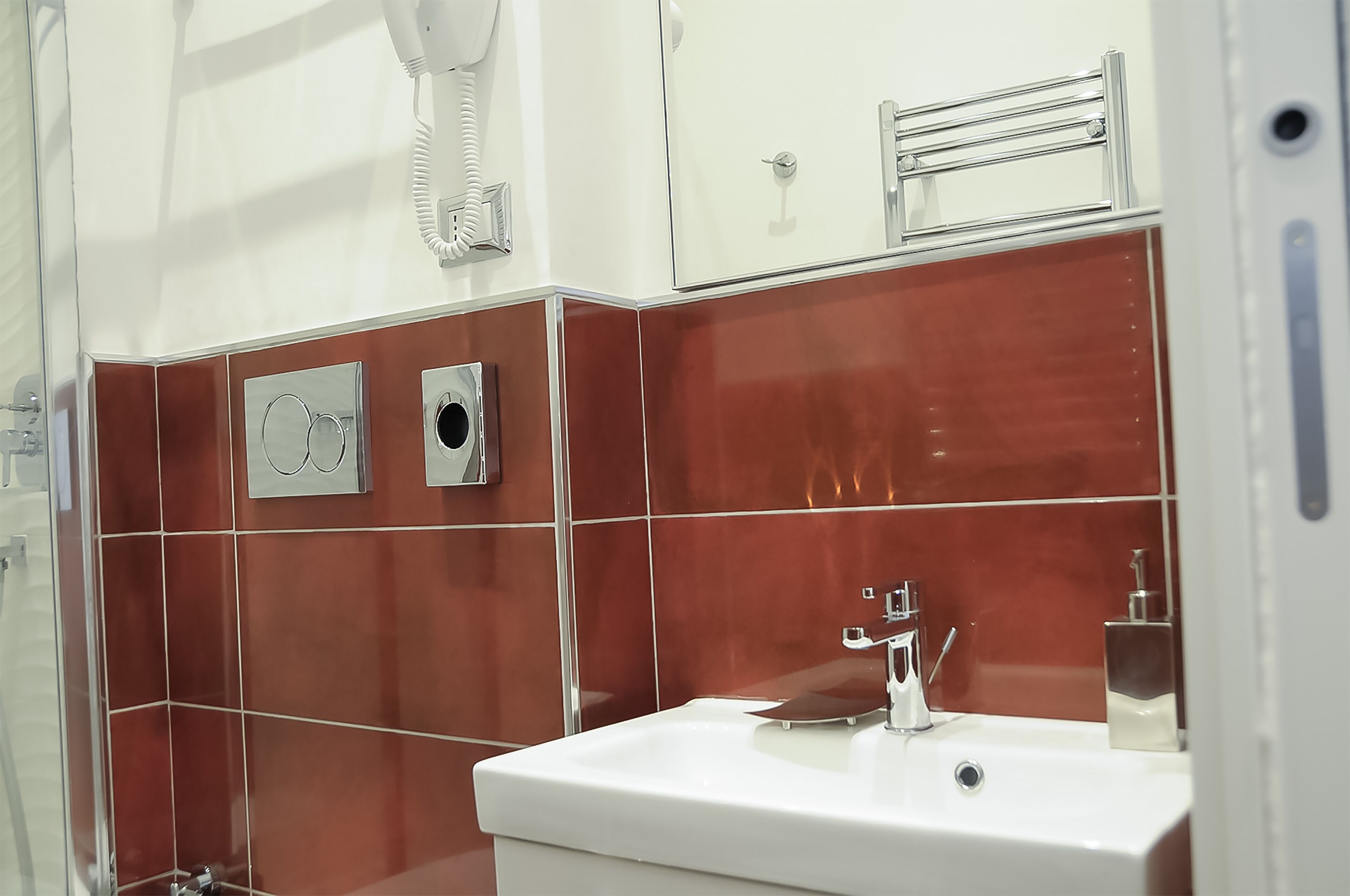 Casa de banho com uma pia branca, torneiras cromadas e paredes com azulejos vermelhos.