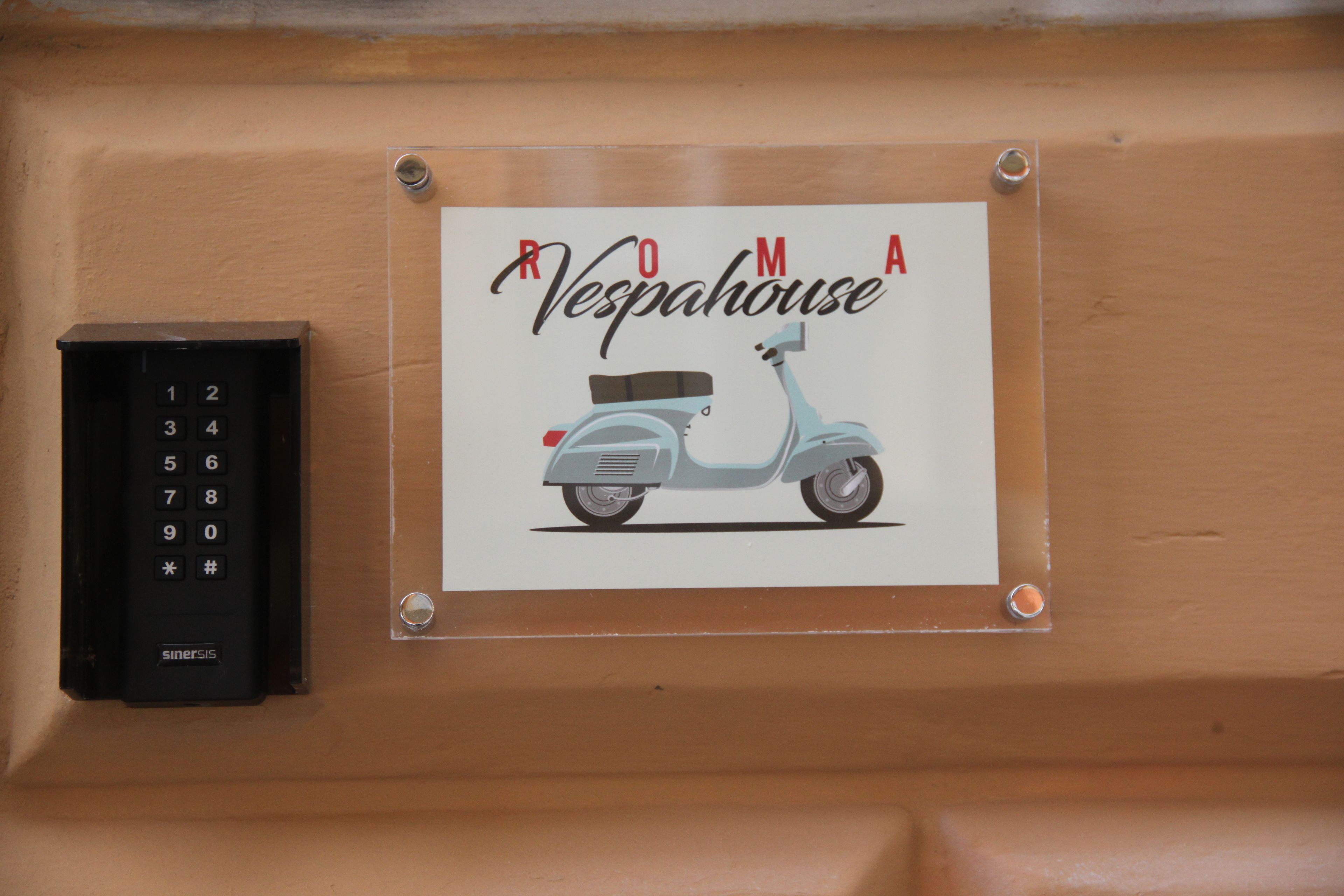 Placa da Vespahouse com ilustração de Vespa e um teclado numérico à esquerda.