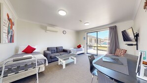 Quarto de hotel com duas camas de solteiro, um sofá, uma mesa de jantar e uma televisão.