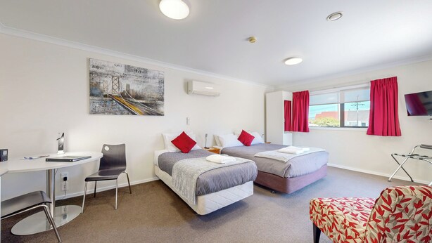 Quarto de hotel com duas camas, uma escrivaninha, uma cadeira, uma televisão e um quadro na parede.