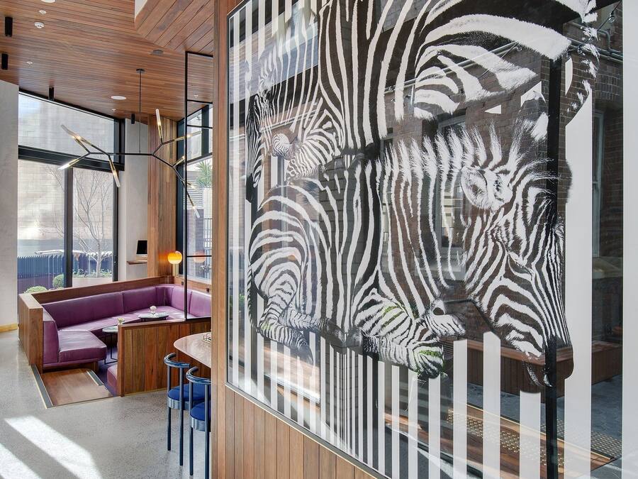 Um interior moderno com um grande mural de zebra, painéis de madeira, um sofá roxo e uma área de jantar com cadeiras azuis.