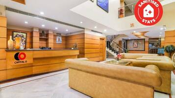 Um saguão de hotel com balcão de recepção, sofás e escada.