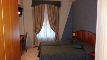Quarto de hotel com duas camas, uma mesa, uma cadeira e uma televisão.