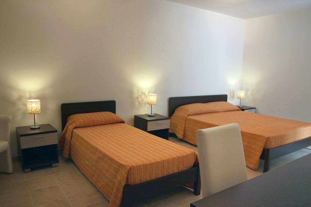 Quarto de hotel com duas camas de solteiro, mesas de cabeceira com abajures, uma escrivaninha e uma cadeira.