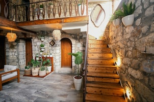 Um interior rústico com escada de madeira, paredes de pedra e diversos vasos de plantas.