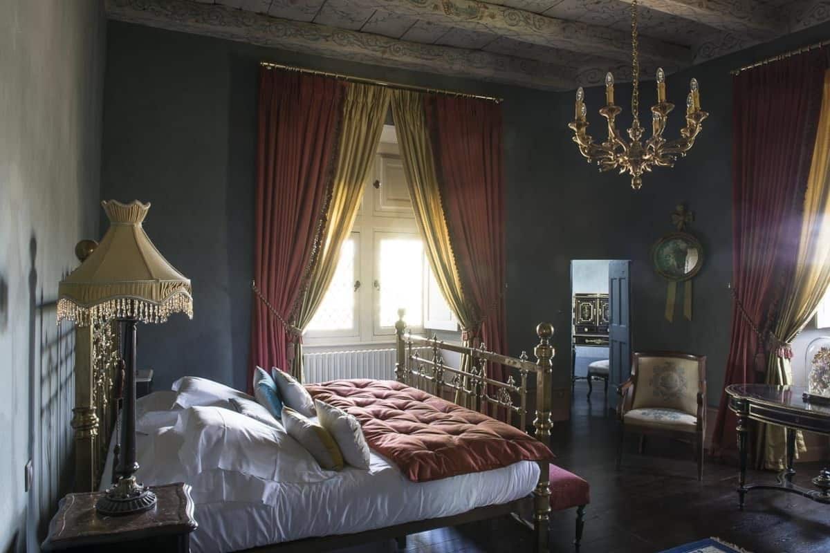 Quarto clássico com cama de dossel, candelabro e cortinas vermelhas.