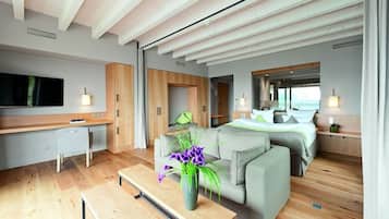 Quarto de hotel moderno com escrivaninha de madeira, sofá, cama e uma janela grande.