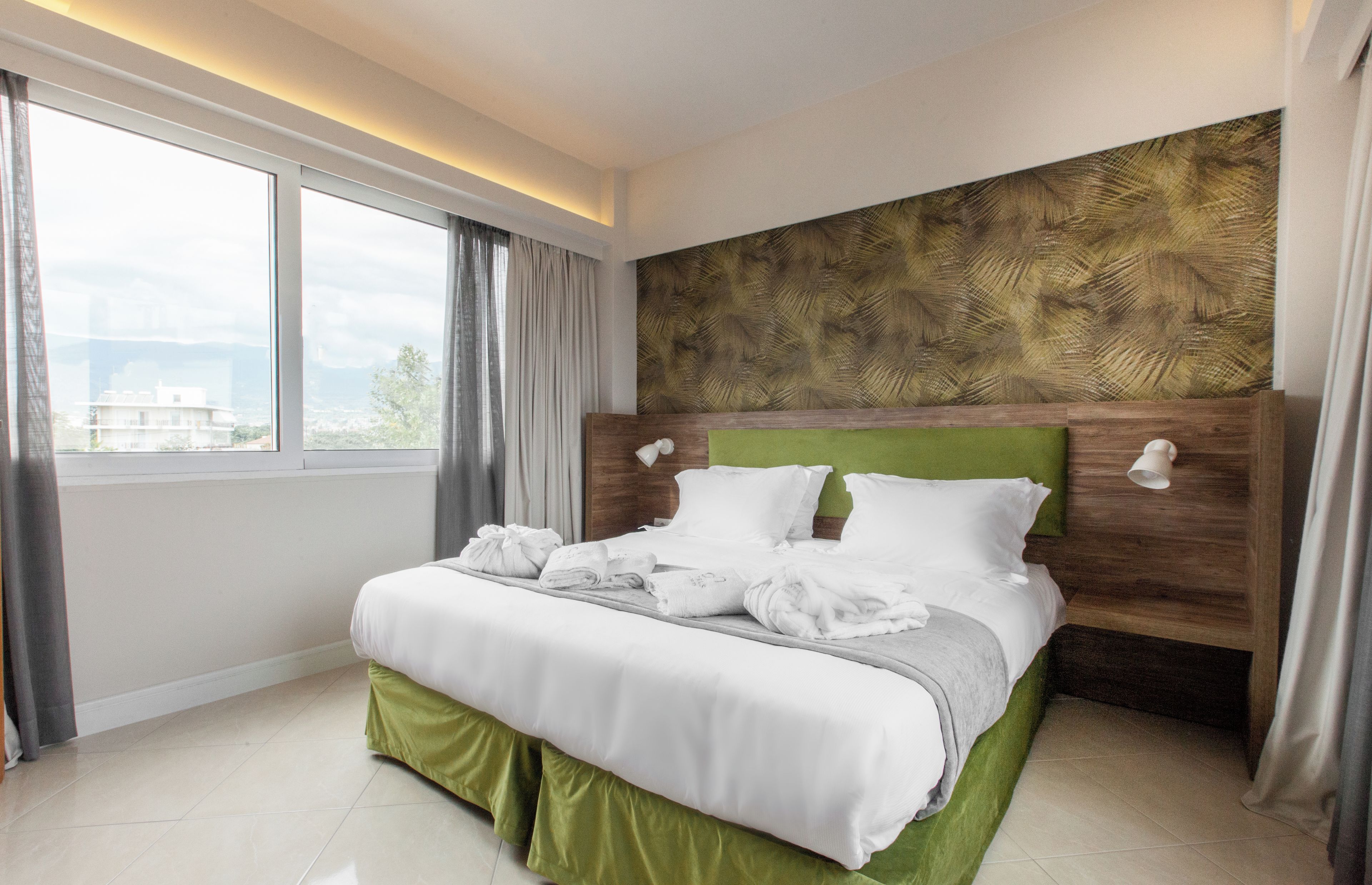 Quarto de hotel com uma cama grande, vista da cidade e cabeceira de madeira.